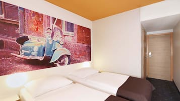 Quarto de hotel com cama, mesa de cabeceira, quadro na parede de uma scooter antiga e porta de madeira.