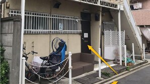 Um edifício com portão fechado, uma bicicleta estacionada do lado de fora e escadas que levam a um andar superior.