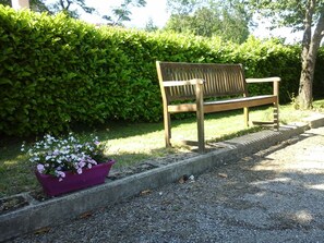 Um banco de madeira em um parque, com uma sebe e um canteiro de flores.