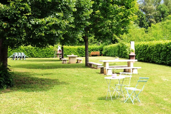 Um jardim com mesas e cadeiras para piquenique, cercado por sebes e árvores.