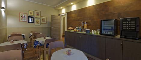 Uma sala de jantar com mesas e cadeiras, um balcão de cozinha com eletrodomésticos e quadros nas paredes.