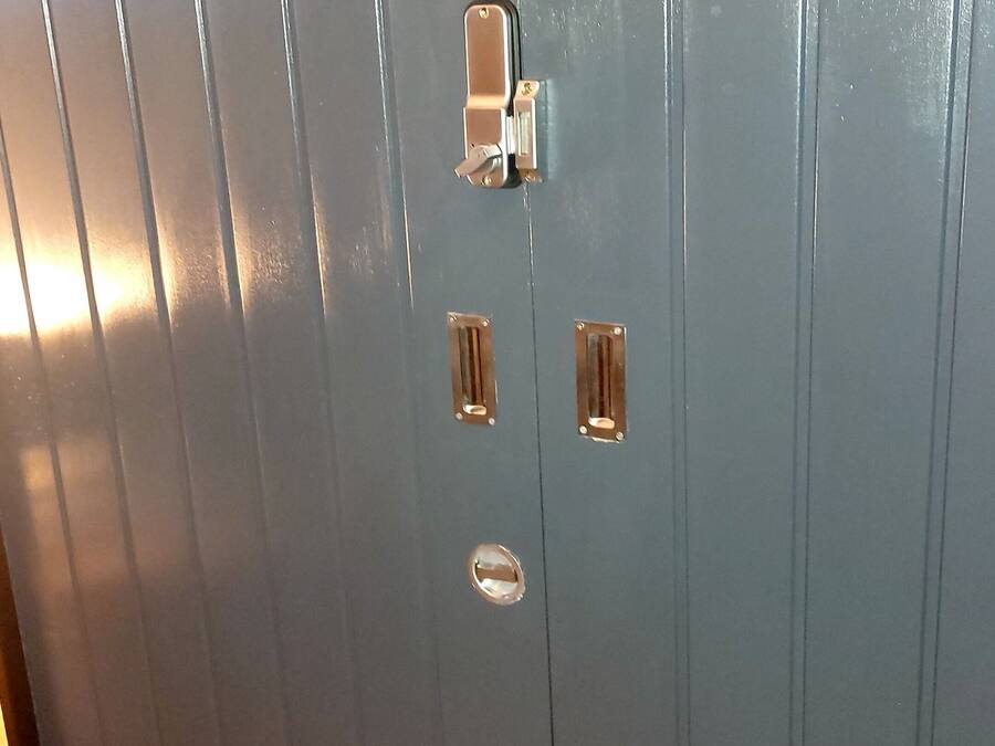 Uma porta cinzenta com uma fechadura, uma fechadela e dois recortes retangulares.