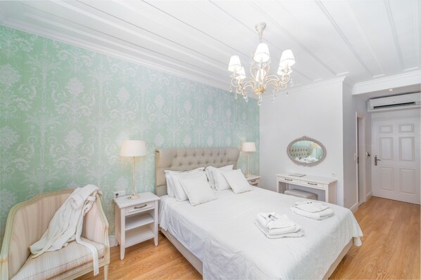 Quarto com uma cama grande, mesas de cabeceira, uma cadeira, um espelho e um guarda-roupa.