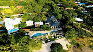 Vista aérea de um resort com piscina, vários edifícios e vegetação exuberante.