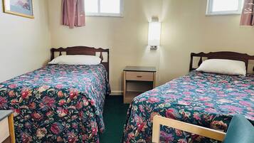 Quarto com duas camas, cada uma com roupa de cama florida, mesa de cabeceira, abajur e janela.