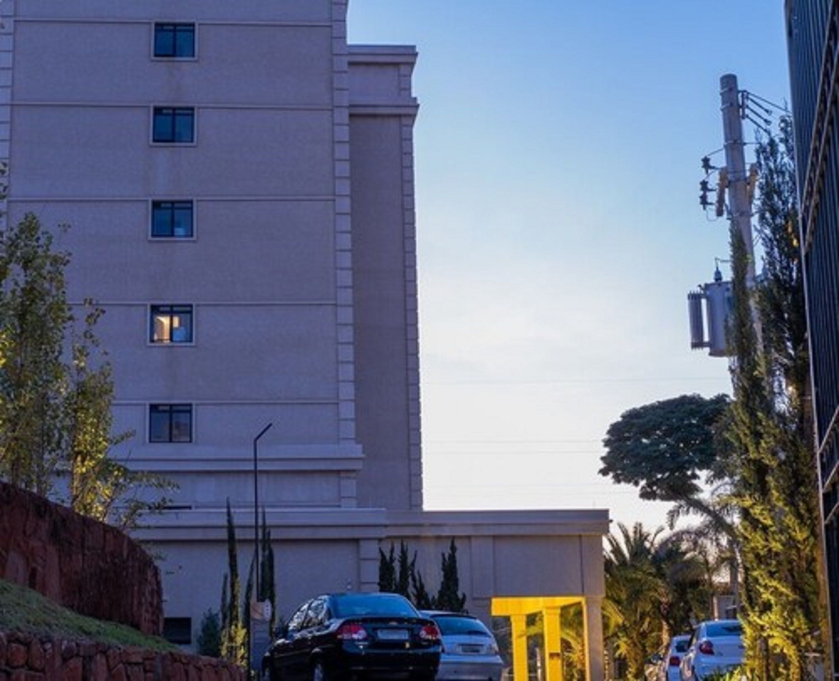 Um edifício de vários andares com fachada plana, diversas janelas e uma área de estacionamento com carros.