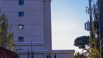 Um edifício de vários andares com fachada plana, diversas janelas e uma área de estacionamento com carros.
