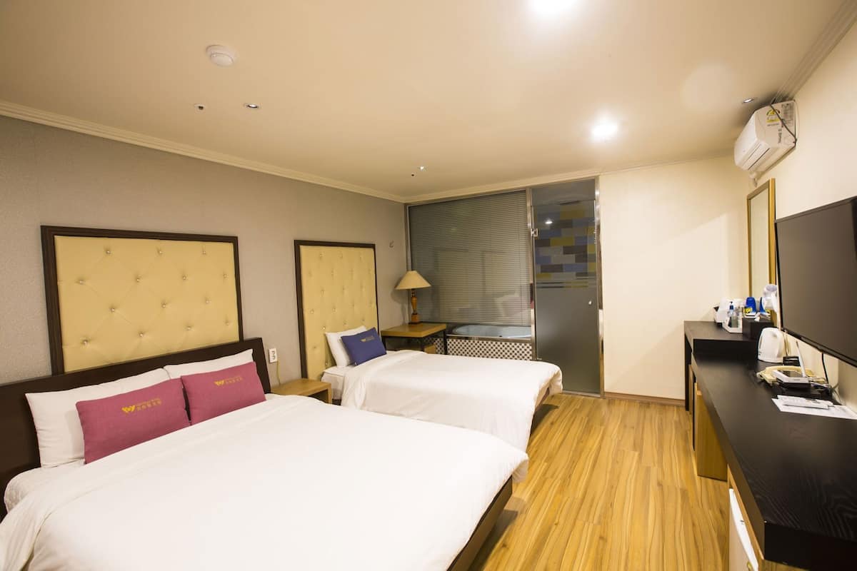 Quarto de hotel com duas camas, uma escrivaninha, televisão e janela com persianas.