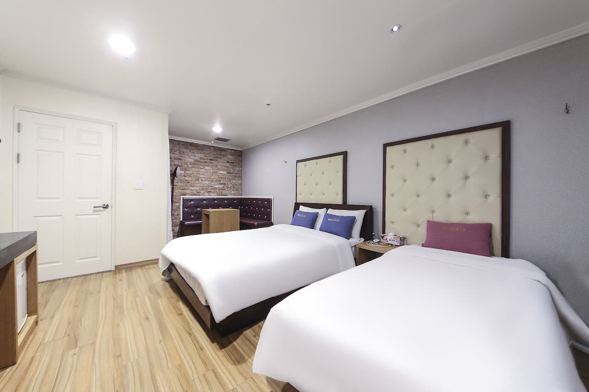 Quarto de hotel com duas camas, uma parede de tijolos e piso de madeira.