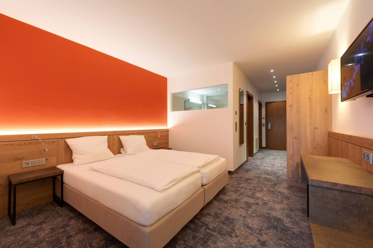 Quarto de hotel moderno com uma cama grande, mesa de cabeceira, televisão montada na parede e painel de parede em madeira.