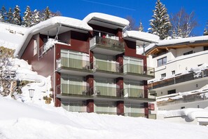 Um hotel com vários andares e varandas, em um cenário coberto de neve, sob um céu azul e límpido.