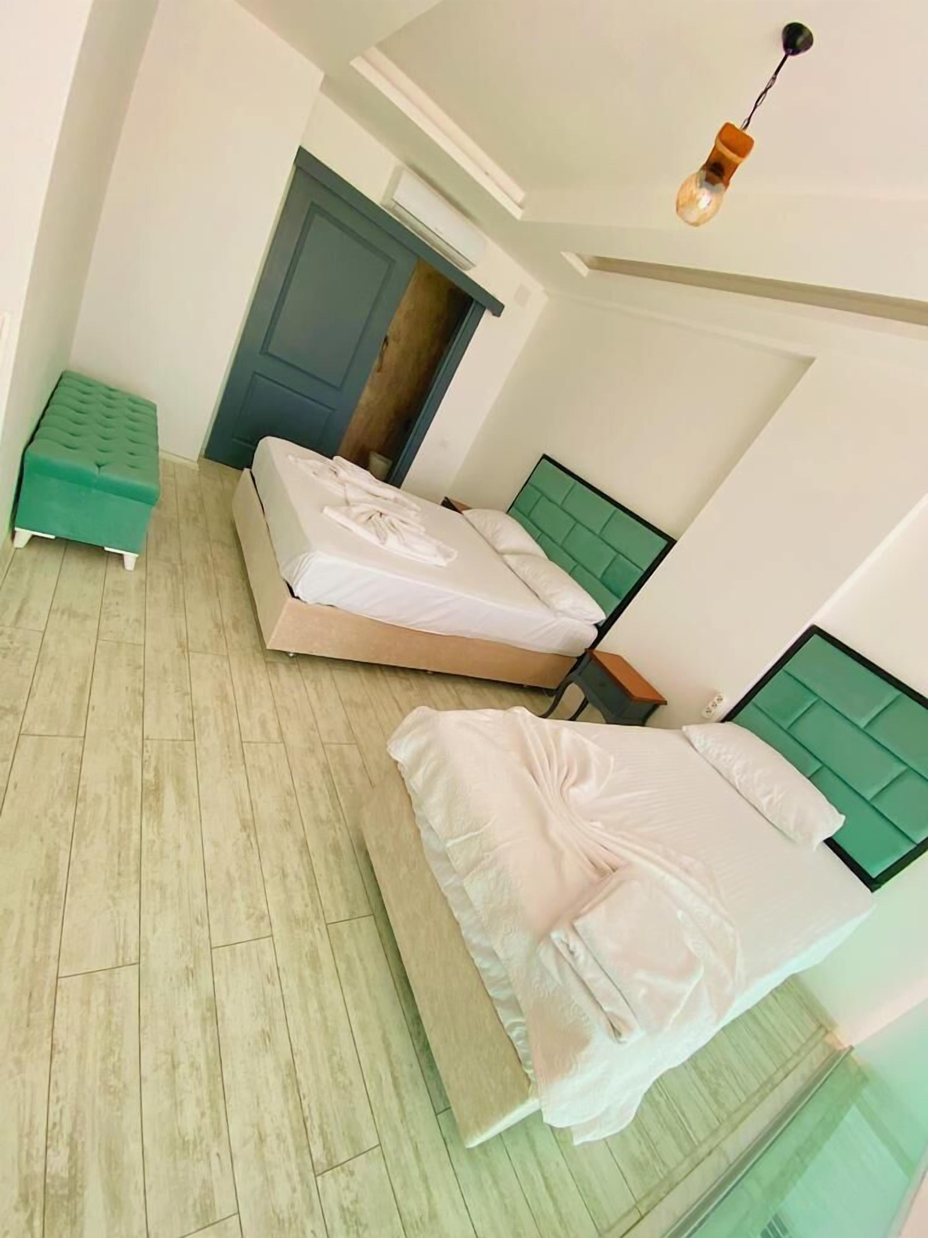 Quarto com duas camas, um banquinho verde e um lustre.