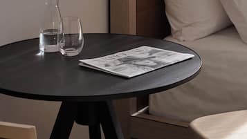 Uma mesa redonda pequena com duas taças, uma garrafa, uma revista e um sofá com almofadas em um quarto de hotel.