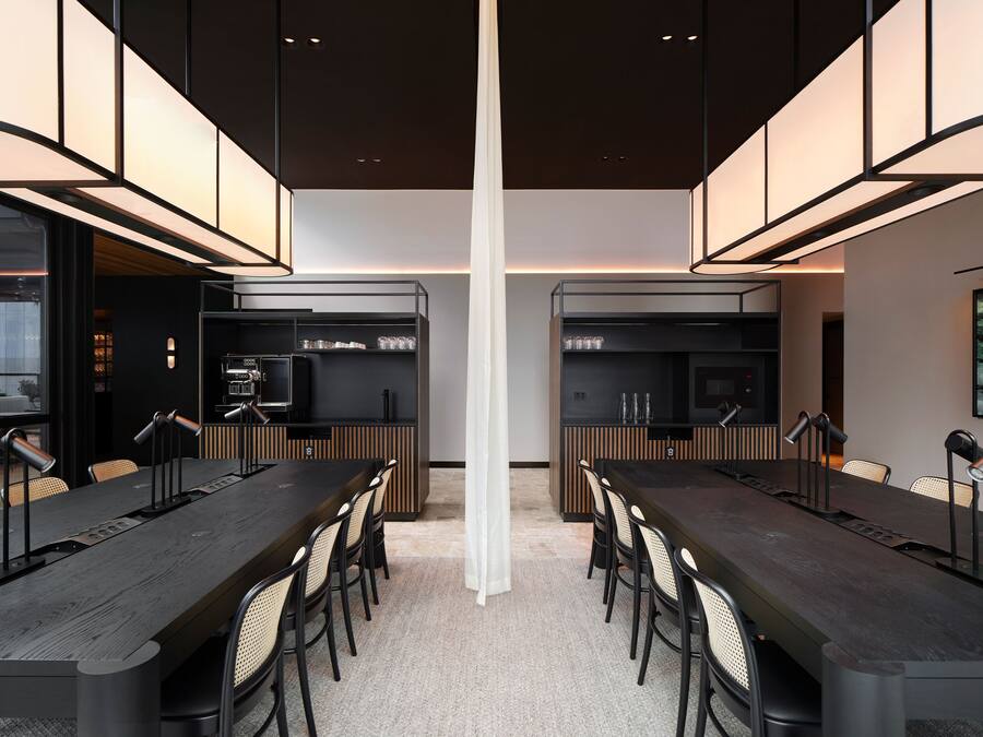 Uma sala de conferências moderna com uma mesa comprida, cadeiras e iluminação pendente.