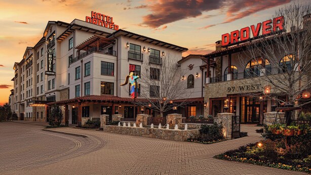 Um hotel com uma placa grande e visível do 'Hotel Drover', uma fonte ao ar livre espaçosa e uma entrada bem iluminada.