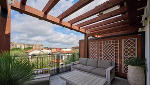 Uma varanda com pérgola de madeira, um sofá, uma mesa e plantas em vasos.