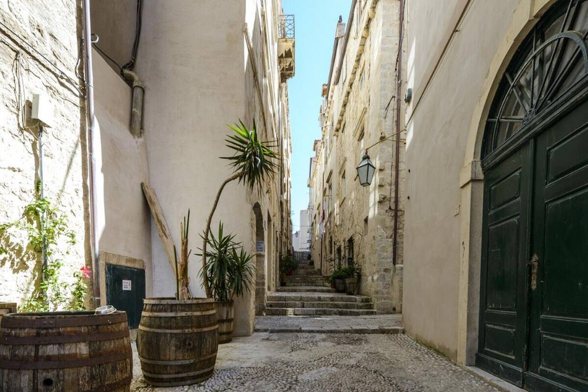 Uma ruela estreita com calçada de pedras, ladeada por edifícios com janelas em arco e uma porta verde.
