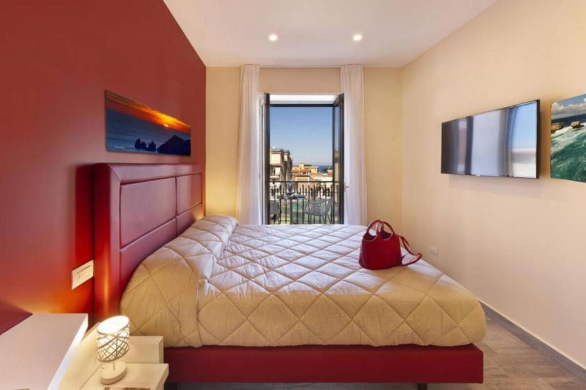 Quarto moderno com uma cama grande, vista da cidade através de uma varanda e uma televisão na parede.