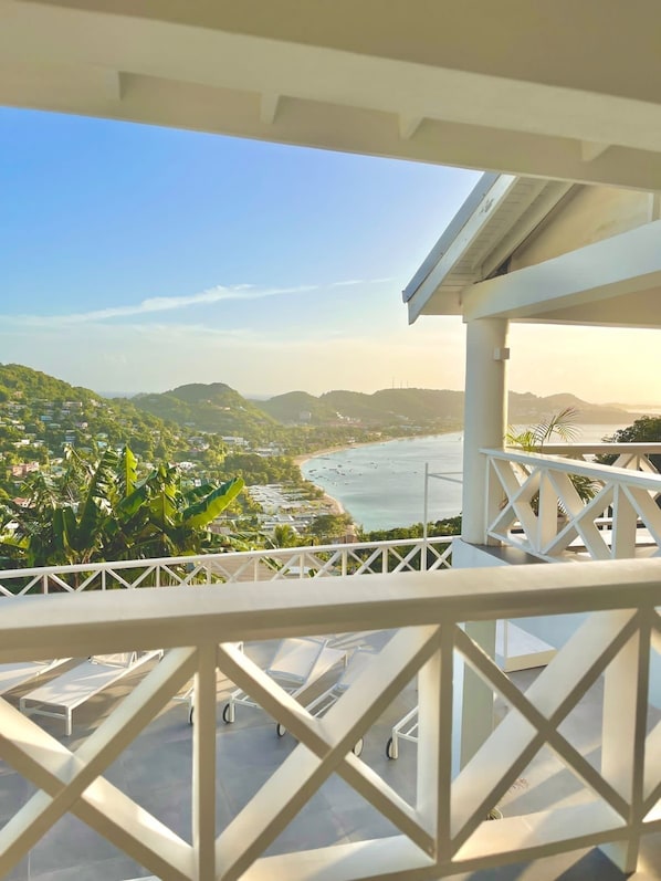 Uma varanda com vista para a paisagem costeira, incluindo colinas, uma praia e barcos.
