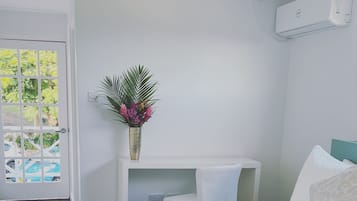 Quarto com cama, escrivaninha, vaso com flores e ar condicionado.