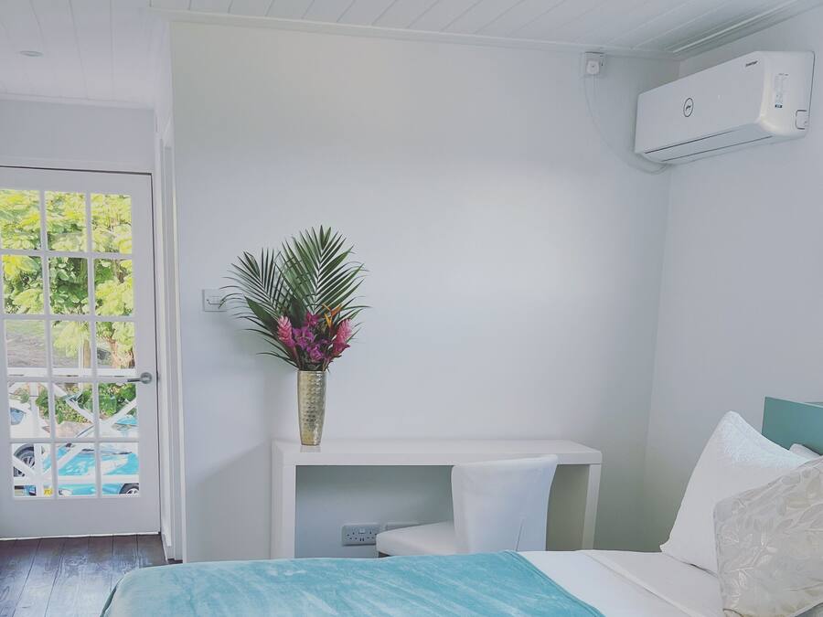 Quarto com cama, escrivaninha, vaso com flores e ar condicionado.