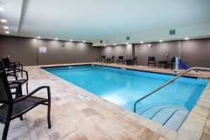 Piscina interna com marcação de profundidade de 3 pés, rodeada por cadeiras pretas e um relógio na parede.