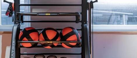Uma academia em casa com um suporte para kettlebells, bolas de medicina e uma bola de exercícios azul.
