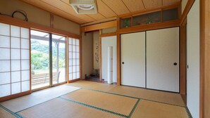 Um quarto japonês tradicional com tatames, portas deslizantes e vista para o verde lá fora.