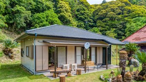 Uma casa com varanda coberta, área de estar externa e um jardim com plantas tropicais.