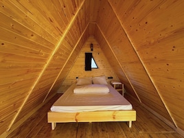 Um quarto de madeira em formato triangular com uma cama, uma mesinha e uma janela.