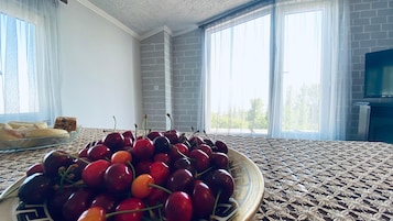 Quarto com uma janela grande, televisão e uma mesa com um prato de cerejas.