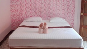 Quarto com uma cama, duas almofadas, um par de sapatos sobre a cama e papel de parede floral.