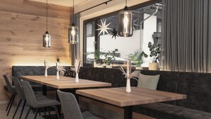 Uma sala de jantar moderna com mesas de madeira e cadeiras cinzentas, um sofá escuro e luminárias pendentes.