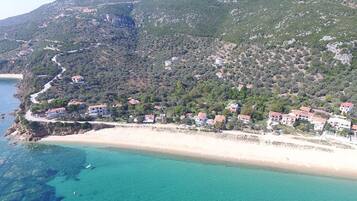 Vista aérea de uma área costeira com praia, casas e montanhas ao fundo.