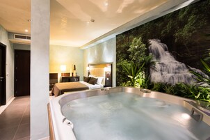 Quarto de hotel moderno com uma banheira grande, uma cama com encosto e um mural na parede com tema de cachoeira.