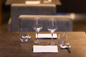 Mesa de madeira escura com três copos de vinho e um garfo.