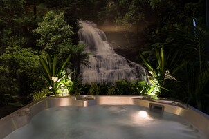 Uma banheira de hidromassagem com um cenário de cachoeira, rodeada por vegetação exuberante.