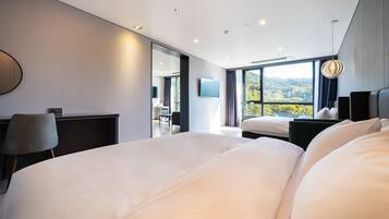 Quarto de hotel moderno com uma cama grande, uma escrivaninha e uma televisão. A janela oferece vista para uma paisagem montanhosa.