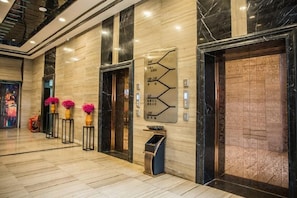 Um saguão de hotel com piso de mármore, um balcão de recepção e um elevador grande.