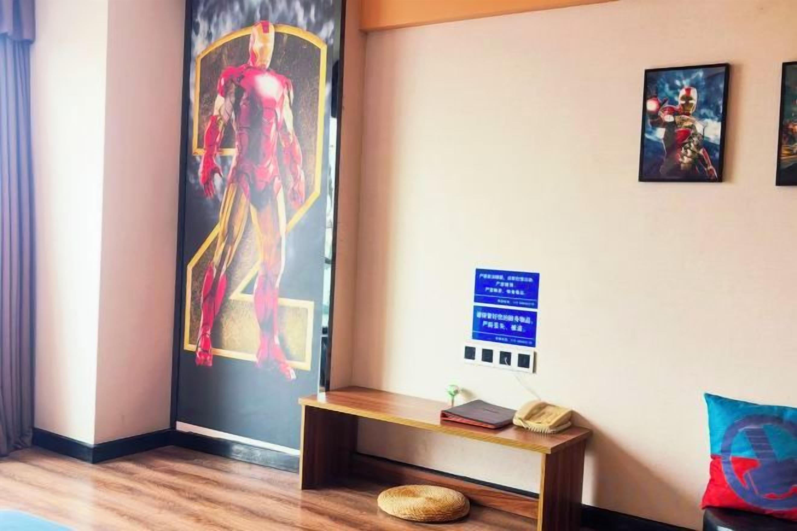 Um saguão de hotel com balcão de recepção, um cartaz de um super-herói e uma placa com informações sobre os quartos.