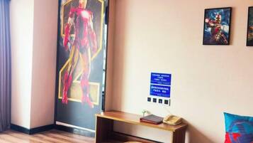 Um saguão de hotel com balcão de recepção, um cartaz de um super-herói e uma placa com informações sobre os quartos.