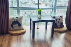 Quarto com vista pela janela, uma mesinha com uma planta e duas almofadas com estampas de animais.