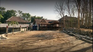 Paisagem rural com construções tradicionais de telhado de palha, chão de terra e uma parede de pedra.