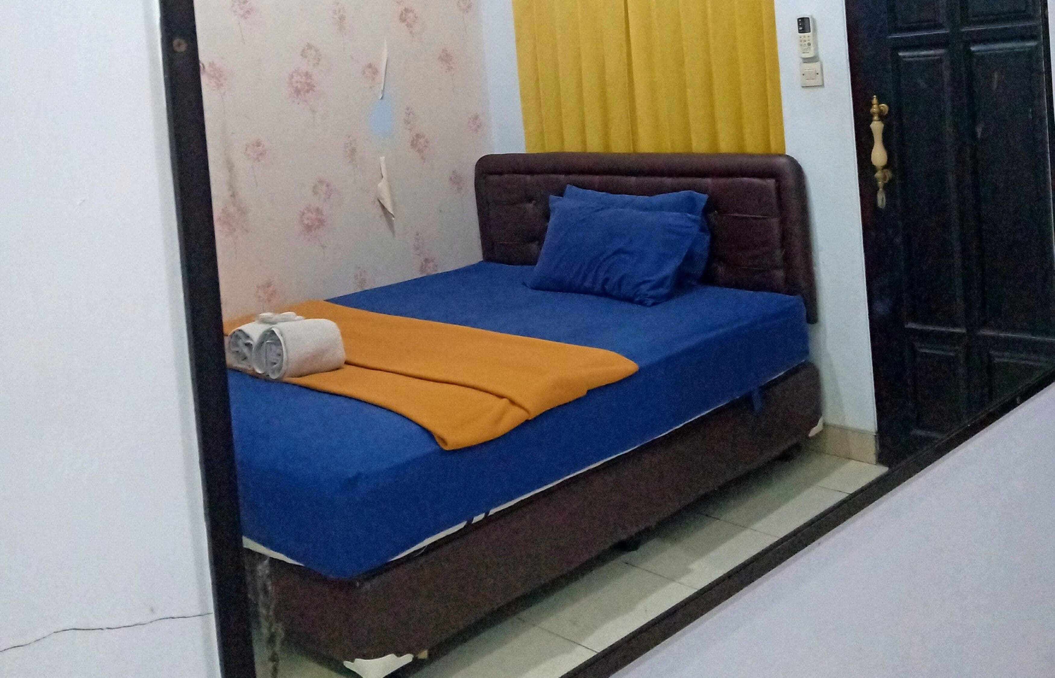 Quarto pequeno com uma cama de solteiro, colcha azul, cabeceira marrom e travesseiro azul.