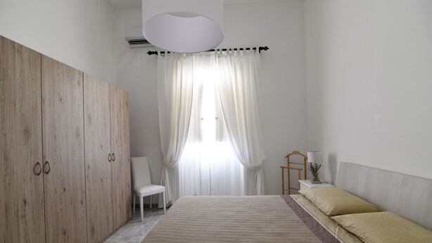 Quarto com cama, guarda-roupa, cadeira e mesa de cabeceira com abajur.