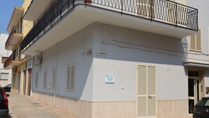 Um edifício com varanda, persianas e uma placa indicando estacionamento.