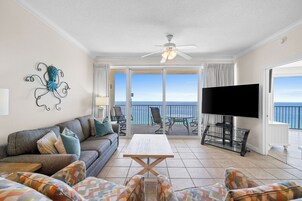 Uma sala de estar com sofá, cadeiras, mesa de centro, TV e varanda com vista para o mar.