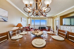 Uma sala de jantar com uma mesa de madeira posta para quatro pessoas, rodeada por cadeiras, e um candelabro acima.