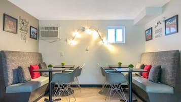 Uma sala de estar moderna com sofá, duas mesas de jantar e cadeiras, uma janela e decorações nas paredes.