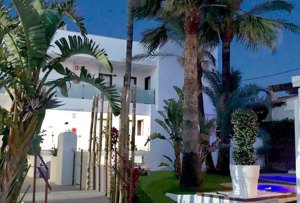 Um edifício moderno com fachada branca, rodeado por palmeiras e um jardim bem cuidado.